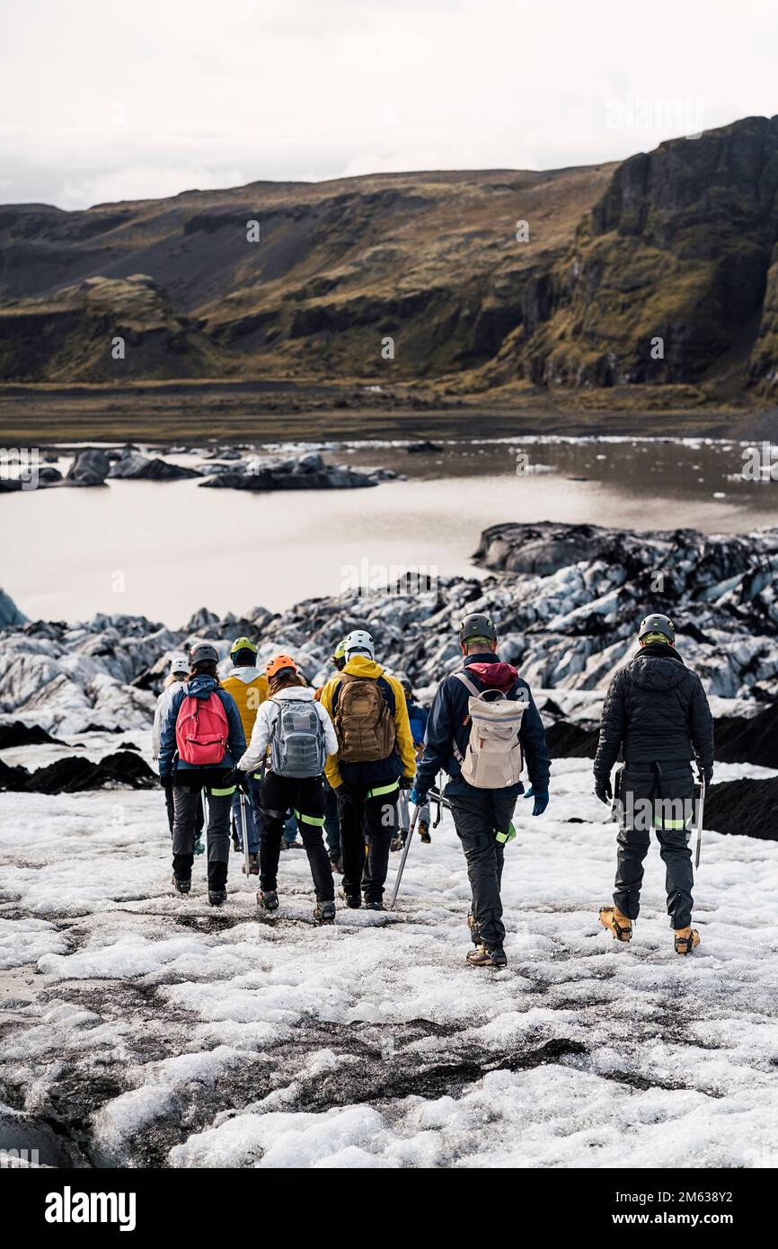 Back view of unrecognizable people in warm clothes and trekking poles ...