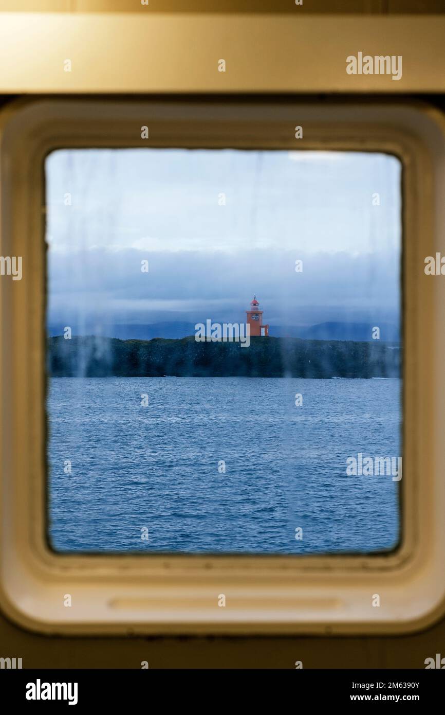 Through window view of rippling sea and lonely lighthouse on rainy day ...