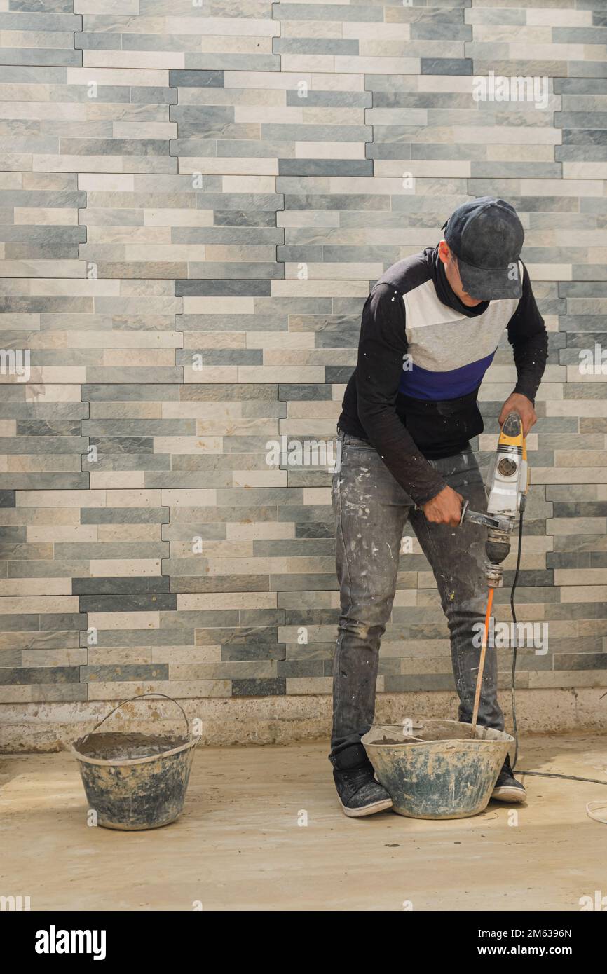 Full body man in dirty clothes using handheld mixer to prepare cement ...