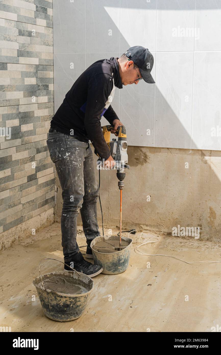 Full body man in dirty clothes using handheld mixer to prepare cement ...