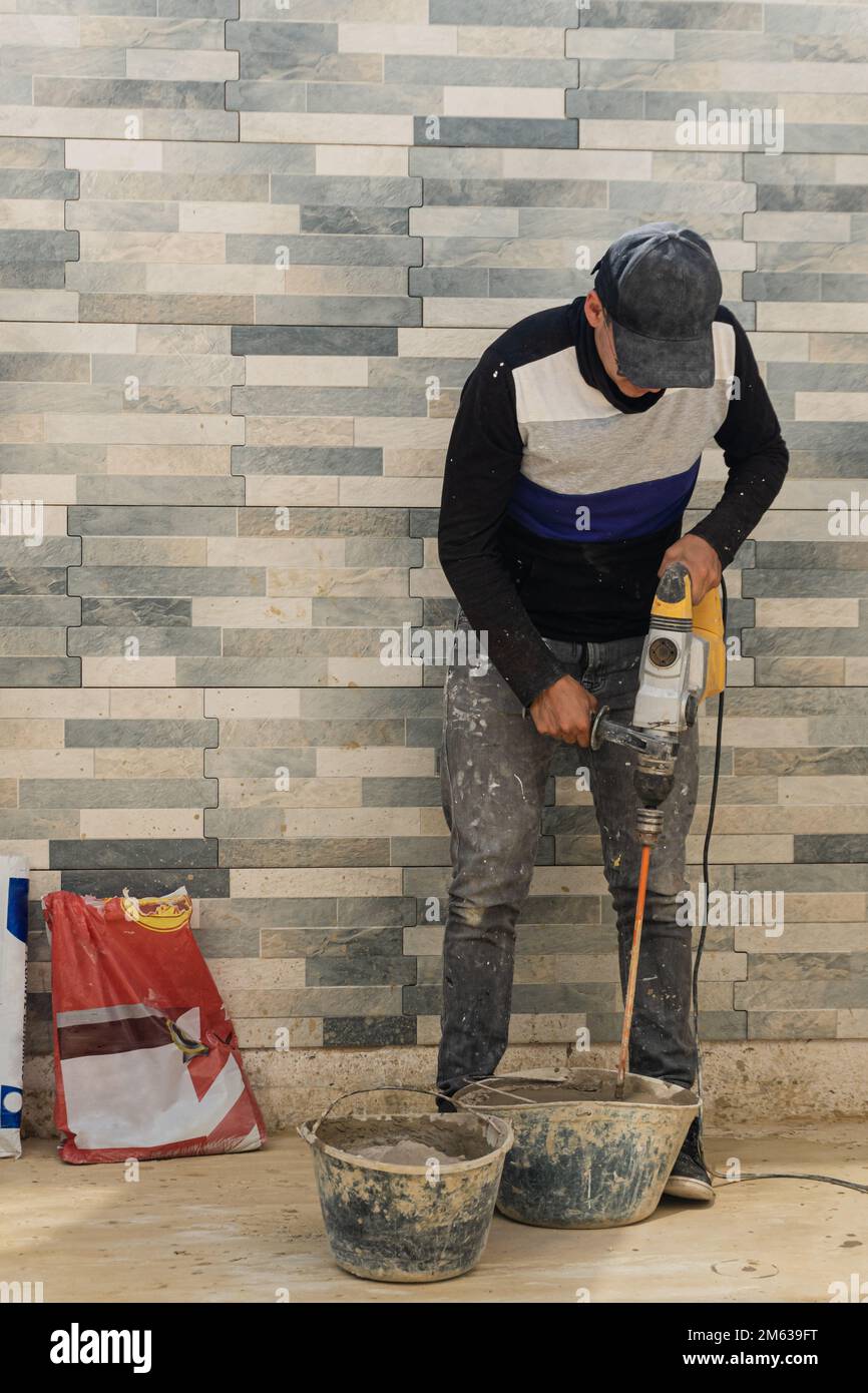 Full body man in dirty clothes using handheld mixer to prepare cement ...