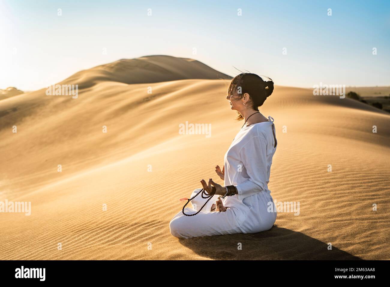 Side view of serene woman in white clothes sitting on sandy ground in ...
