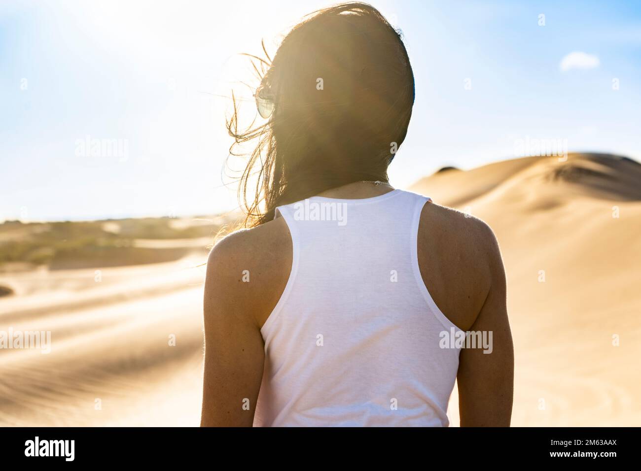 Back view of female in white beach clothes standing on sandy dunes ...