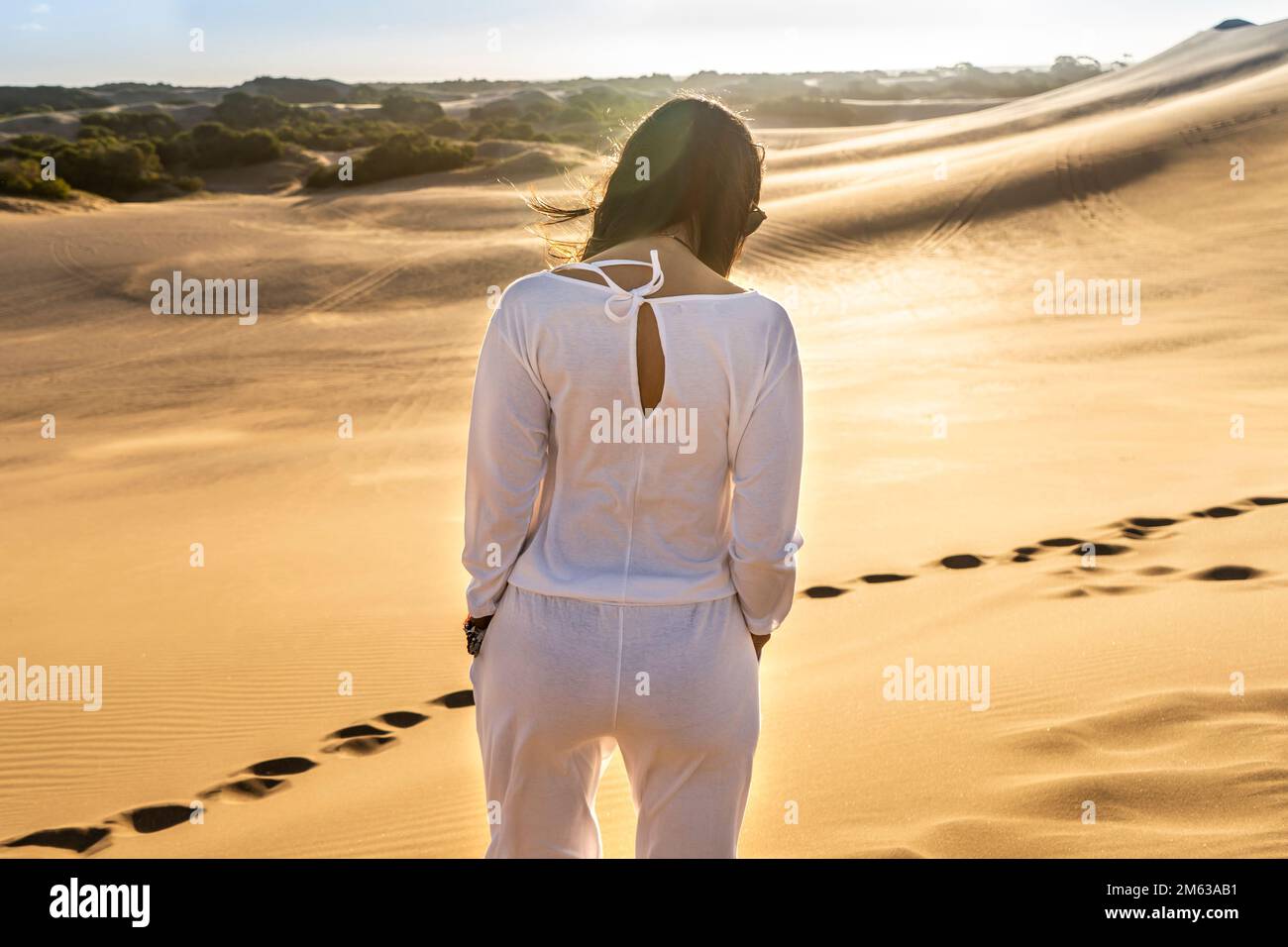 Back view of female in white beach clothes with hands in pockets ...