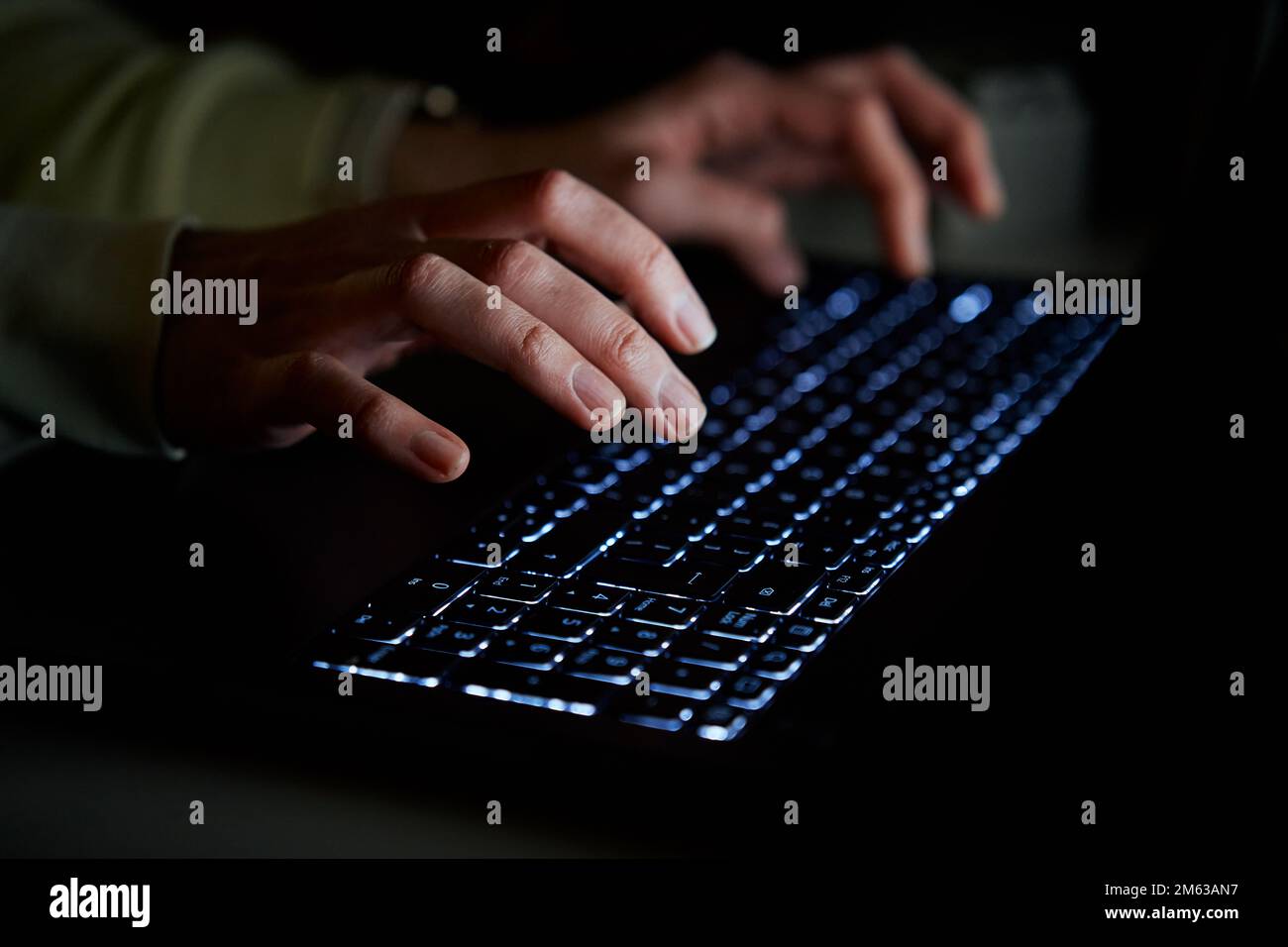 Hands of anonymous person typing on laptop keyboard at night, close up ...
