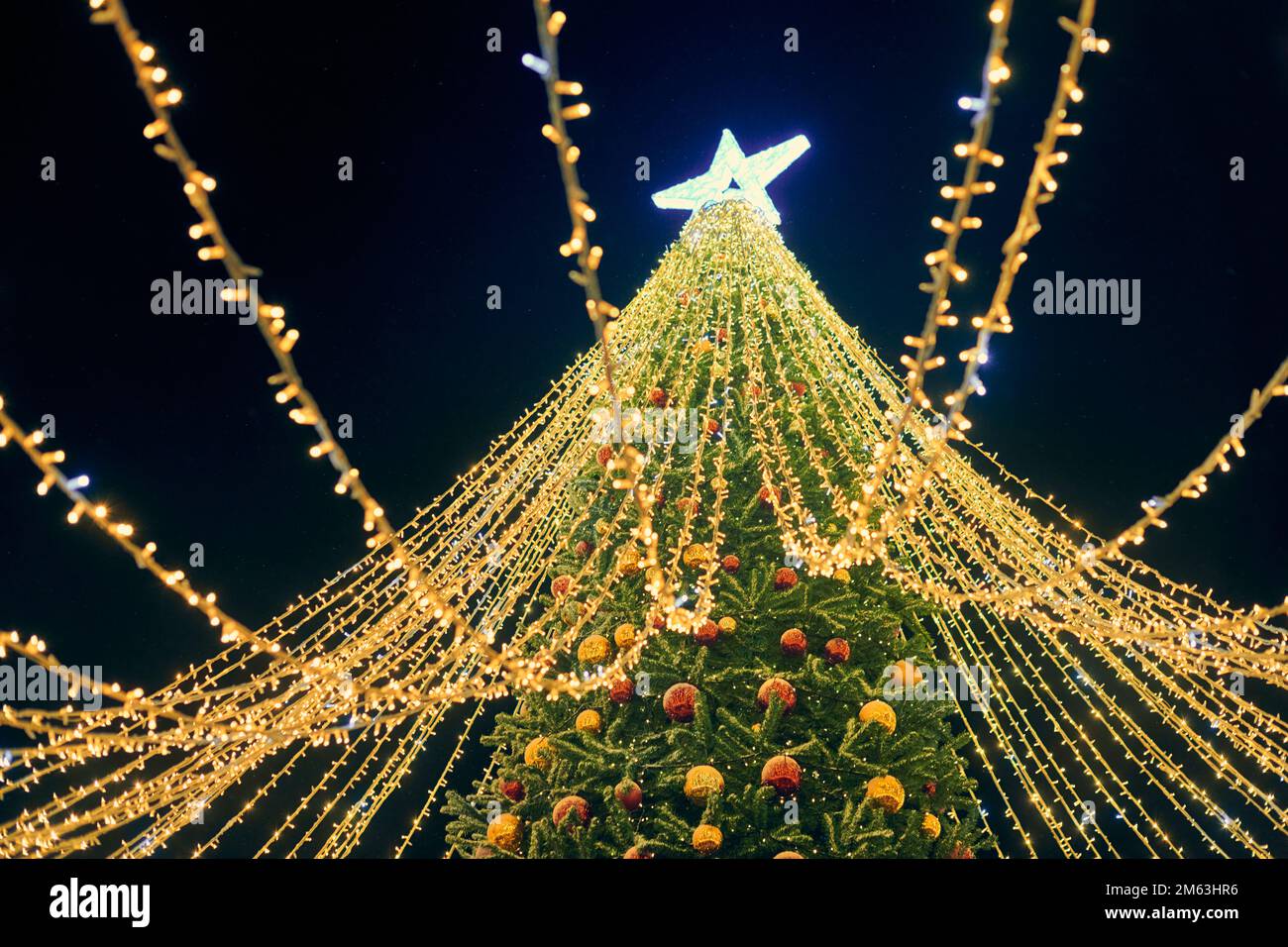 Christmas tree with yellow garlands, decorative bulbs and big white ...
