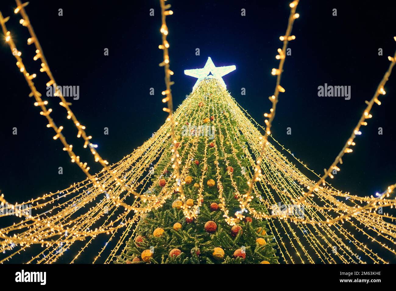 Christmas tree with yellow garlands, decorative bulbs and big white ...