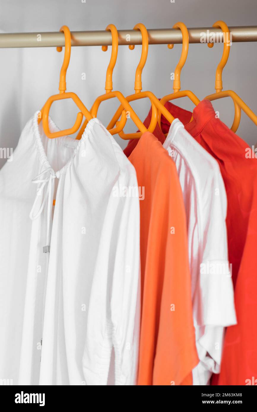 Coral and White colour clothes on hangers. Several blouses, shirts for ...