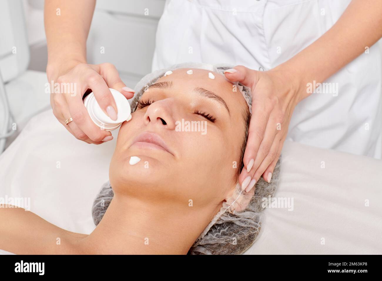 Cosmetologist applying moisturizing cream on woman face for ...