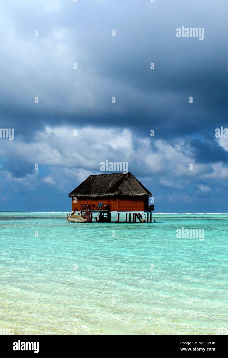 A hut on a beach in the Maldives surrounded by the bright blue waters ...
