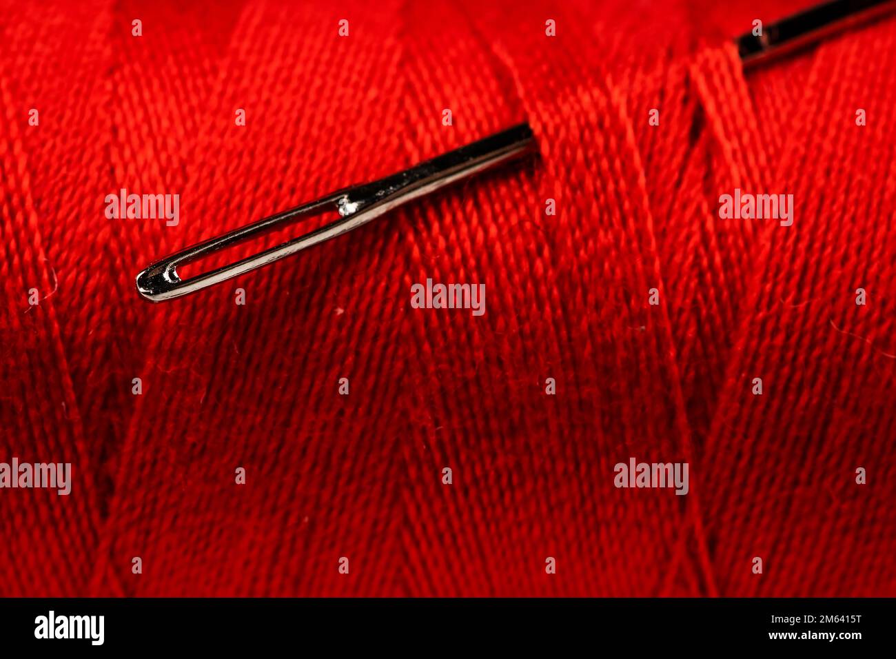 Eye of the needle with red polyester thread. Spool of red polyester ...