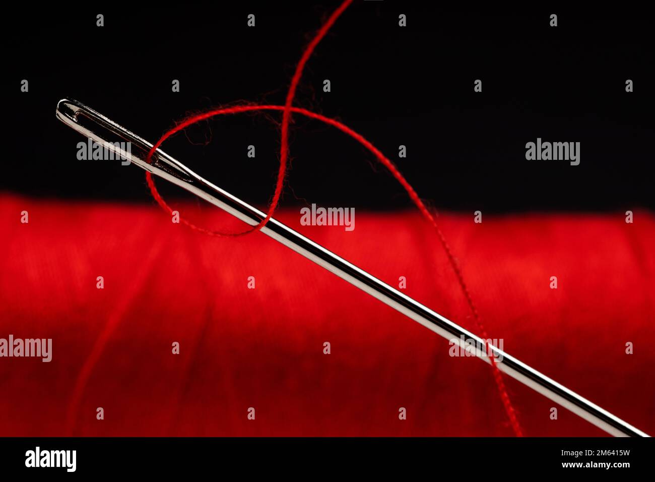 Eye of the needle with red polyester thread. Spool of red polyester ...