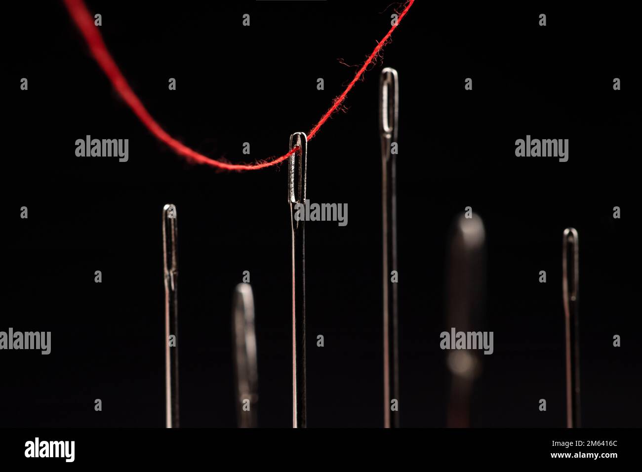 Red thread passing through needles on a black background Stock Photo ...