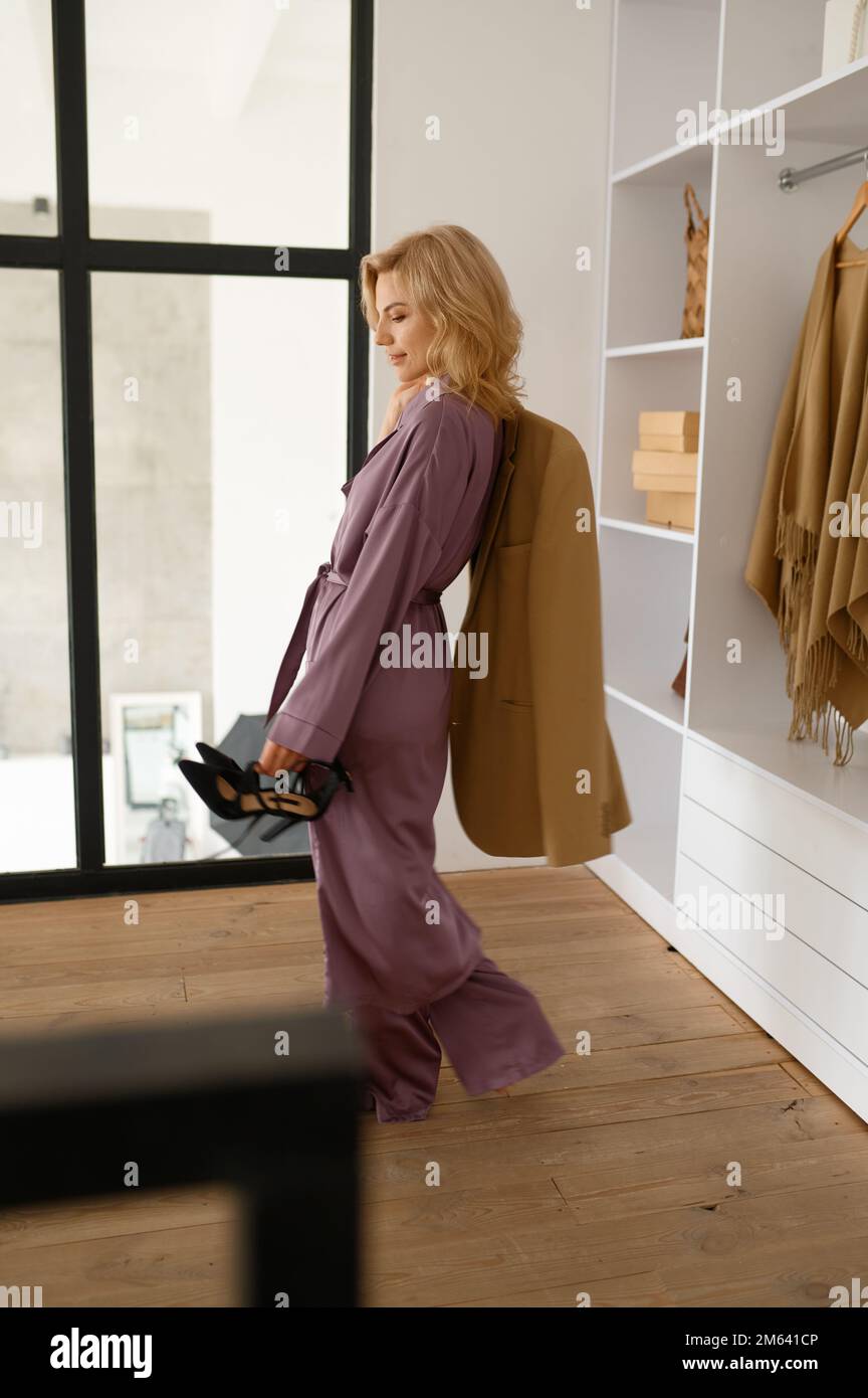 Happy woman in silk nightwear standing with chosen clothes in bedroom ...