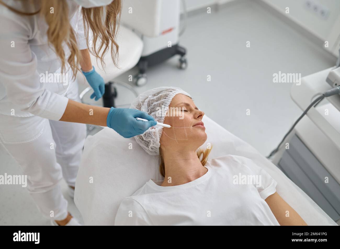 Cosmetologist drawing with white pencil on patient face Stock Photo - Alamy