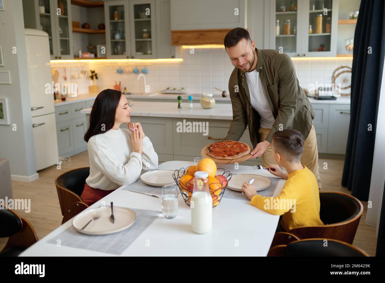 Happy family with child eating pizza sitting at dining table Stock ...