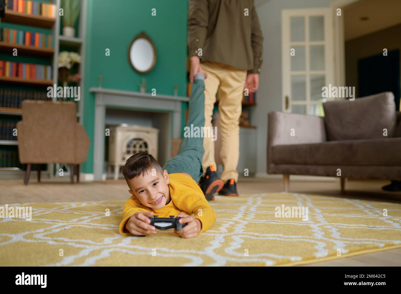 Portrait of smiling son playing video game while father pulling him out ...