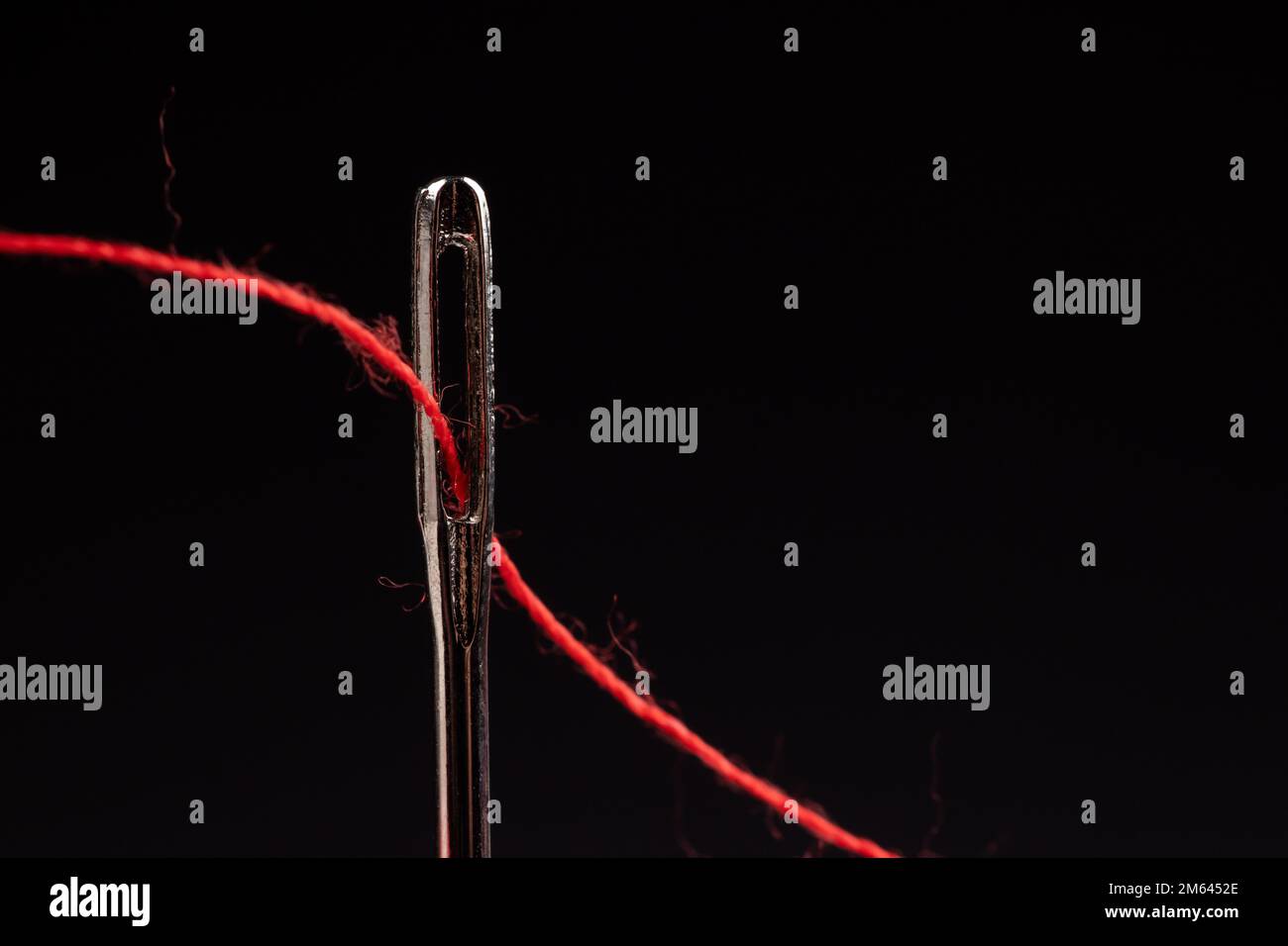 Red thread and needle on black background Stock Photo - Alamy