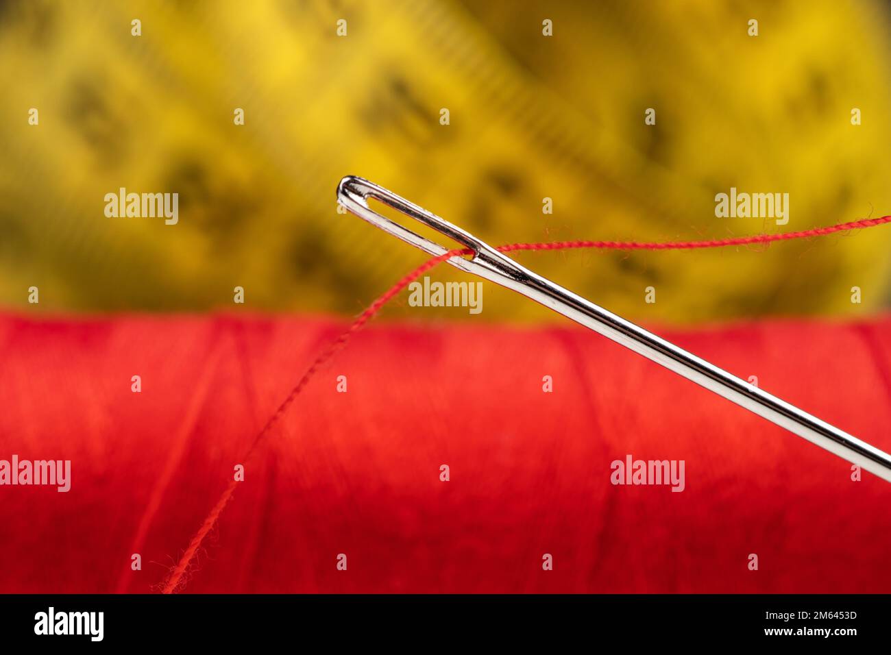 Eye of the needle with red polyester thread. Spool of red polyester ...