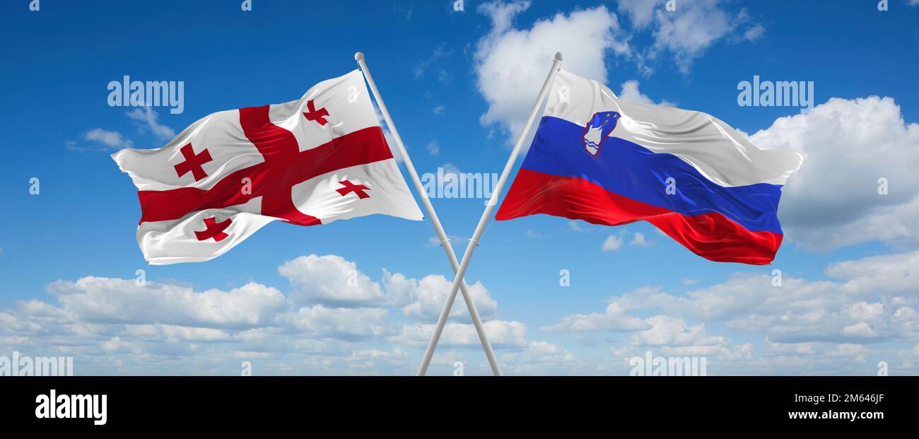 two crossed flags Slovenia and Georgia waving in wind at cloudy sky ...