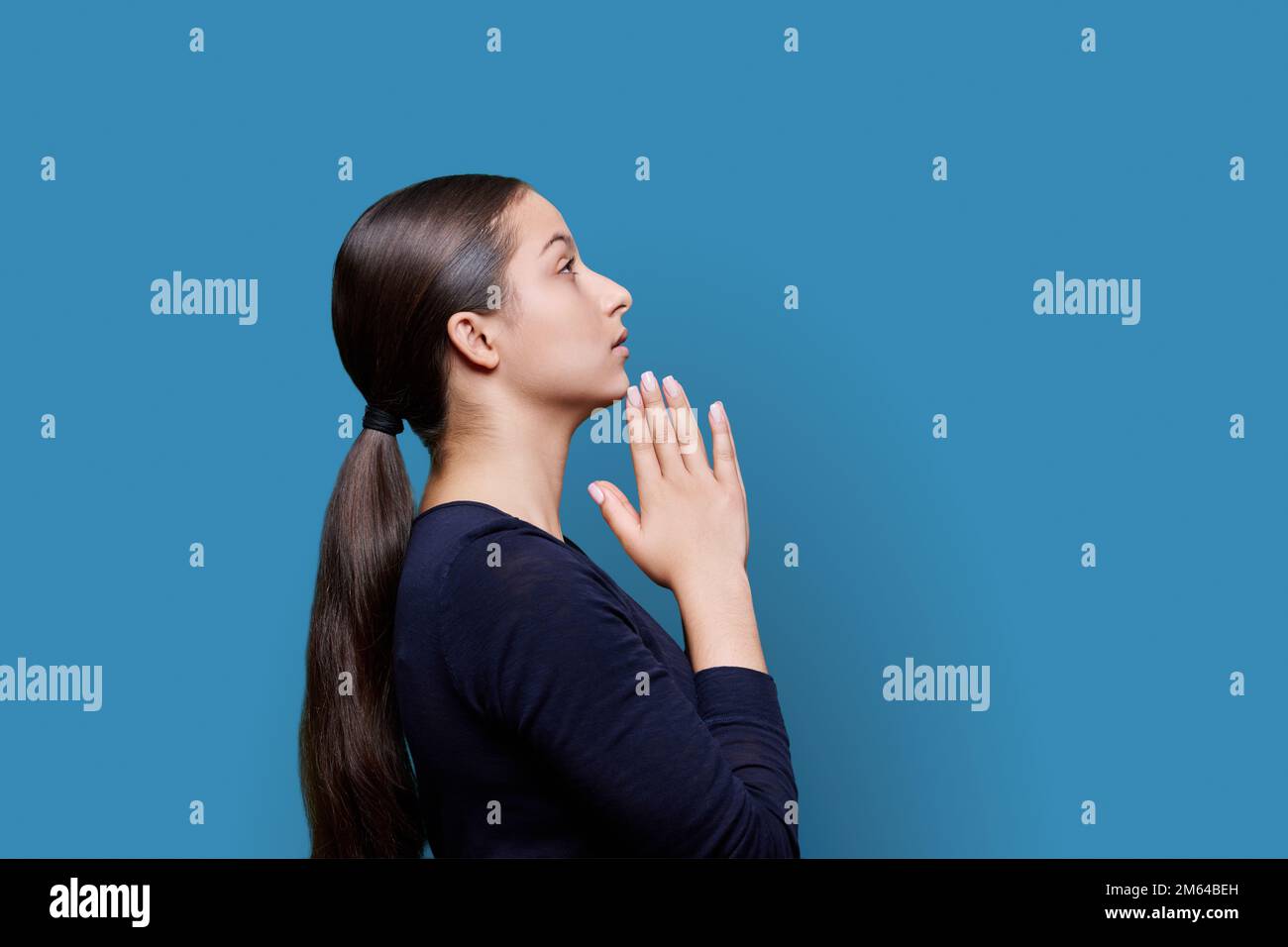 Young female pleading, holding hands in prayer on blue background ...