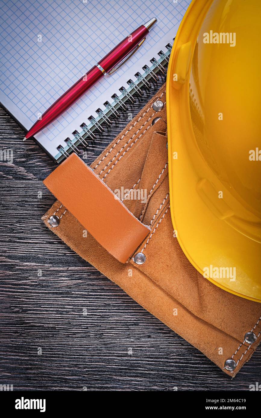 Leather tool belt hard hat checked notepad ball-point pen on wooden ...