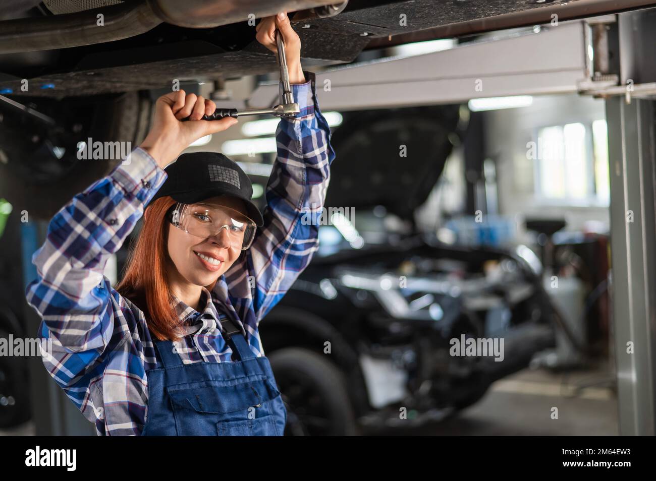 Female mechanic unscrew the nuts on the bottom of the car that is on ...