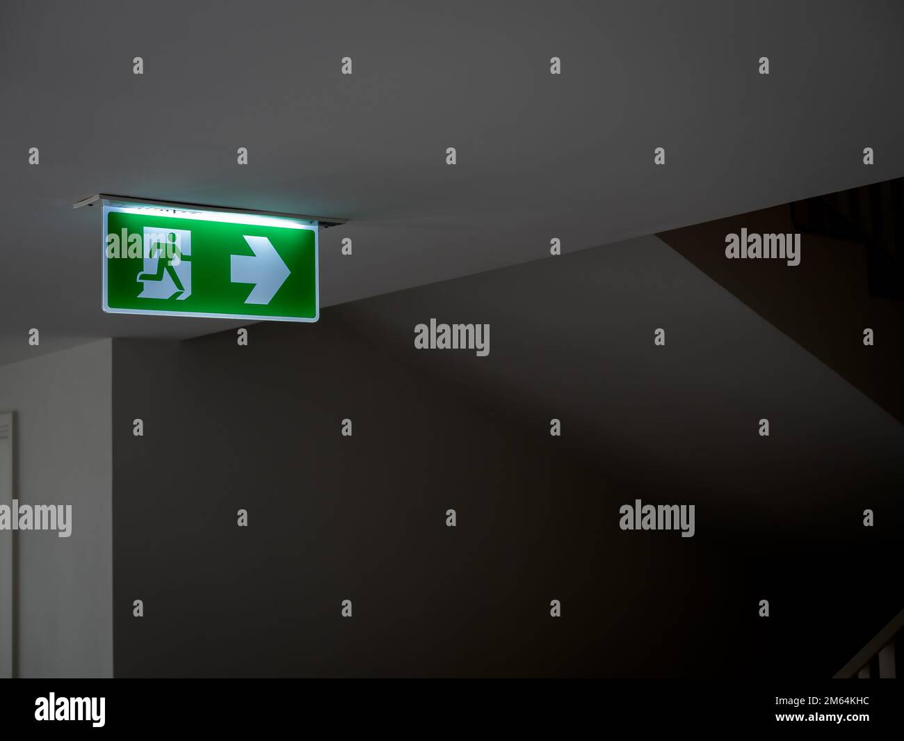 Green fire escape sign hang on the ceiling in the dark building near ...