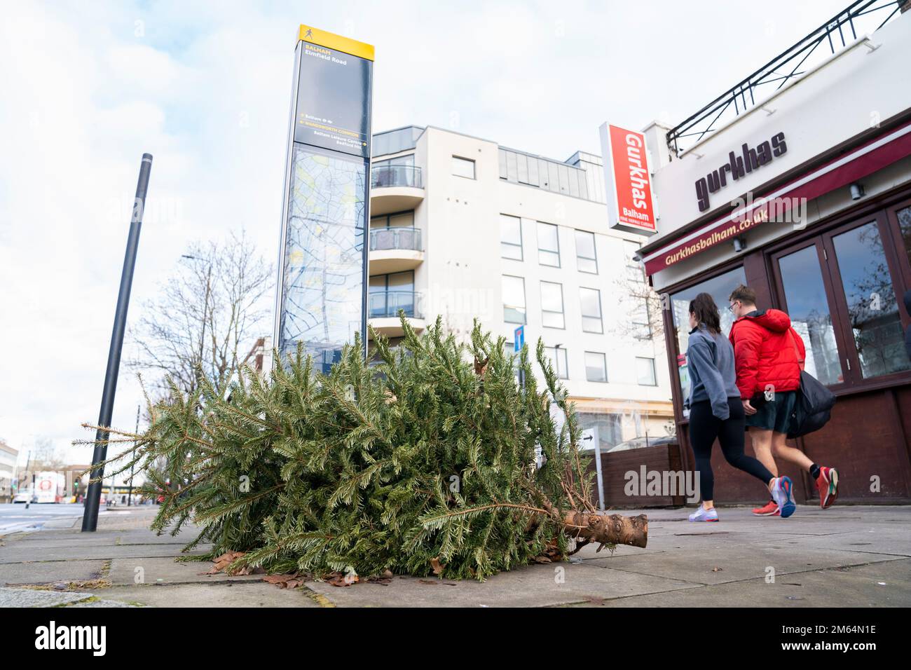 People walk past a Christmas tree discarded on the pavement in Balham, south London. Picture ...