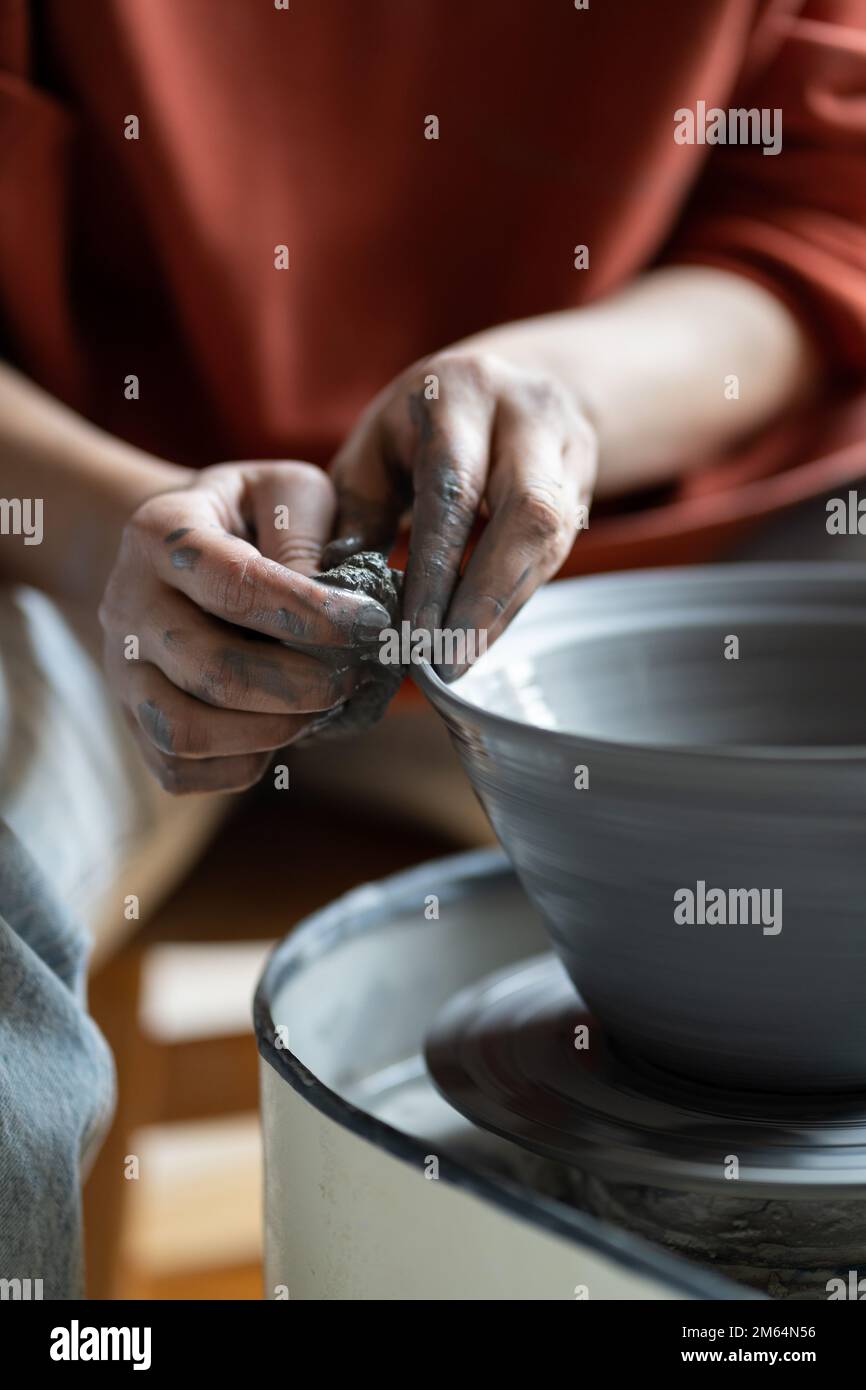 Female potter shaping wet clay on turning wheel into kitchenware in ...