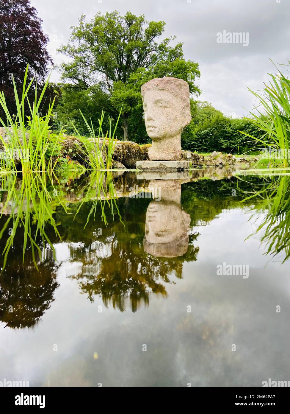 A vertical shot of a stature of a human head reflecting on a water pond ...