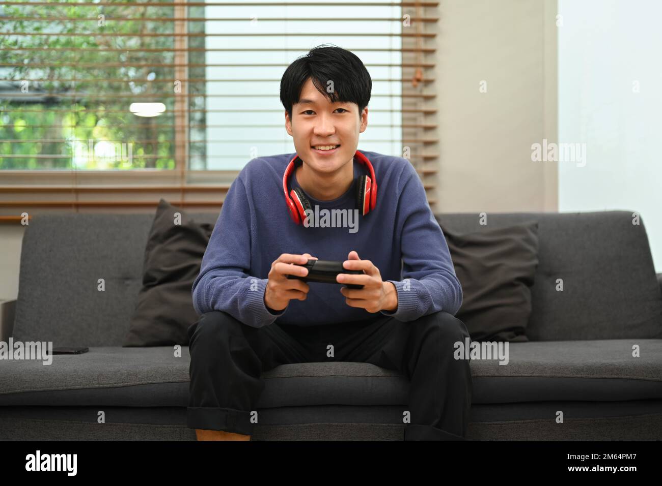 Smiling young asian man playing video game with joystick while sitting ...