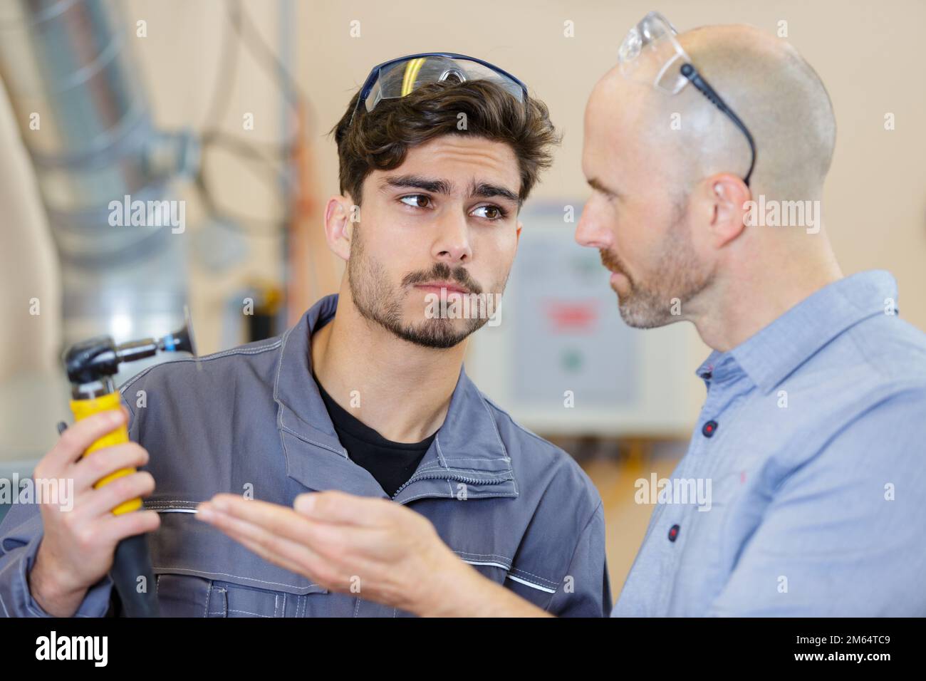 engineer questioning younger worker holding hose Stock Photo - Alamy