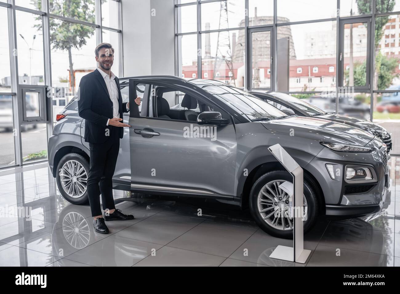 Good-looking salesperson presenting a new vehicle in a car dealership ...