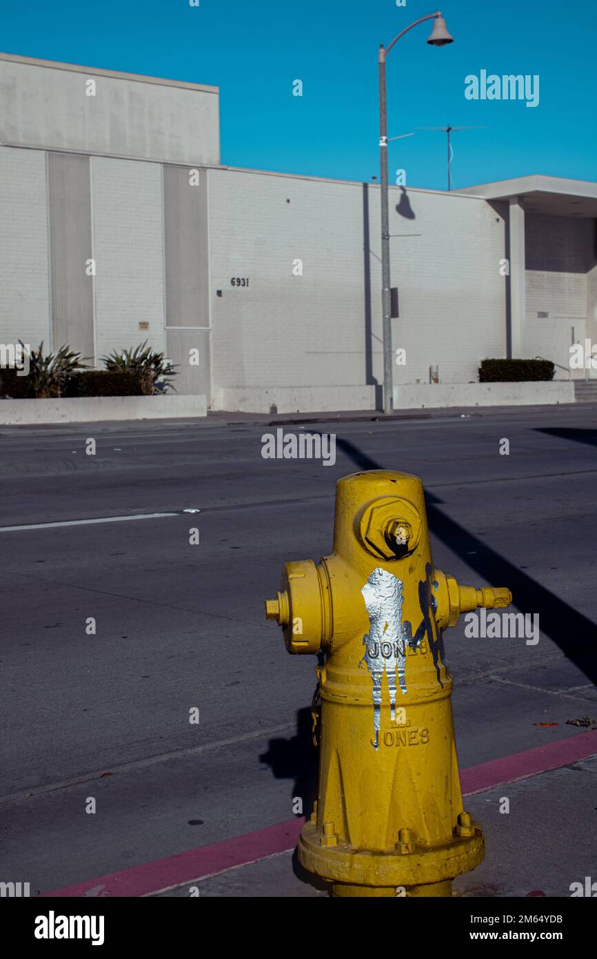 A yellow fire hydrant beside an empty road with white buildings on the ...