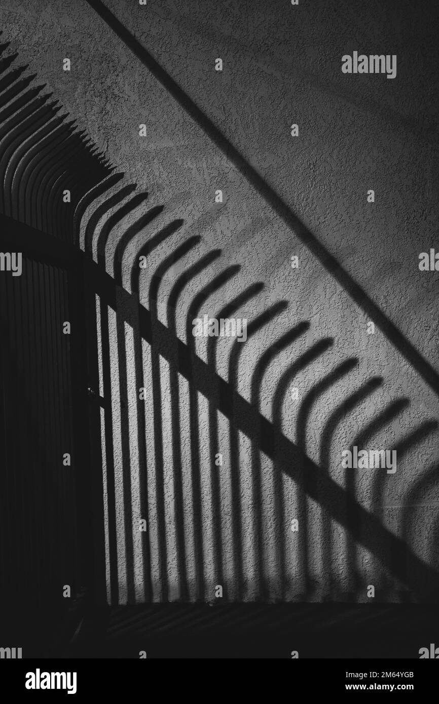 A grayish-white wall under a flashlight with the shadow of a fence cast ...