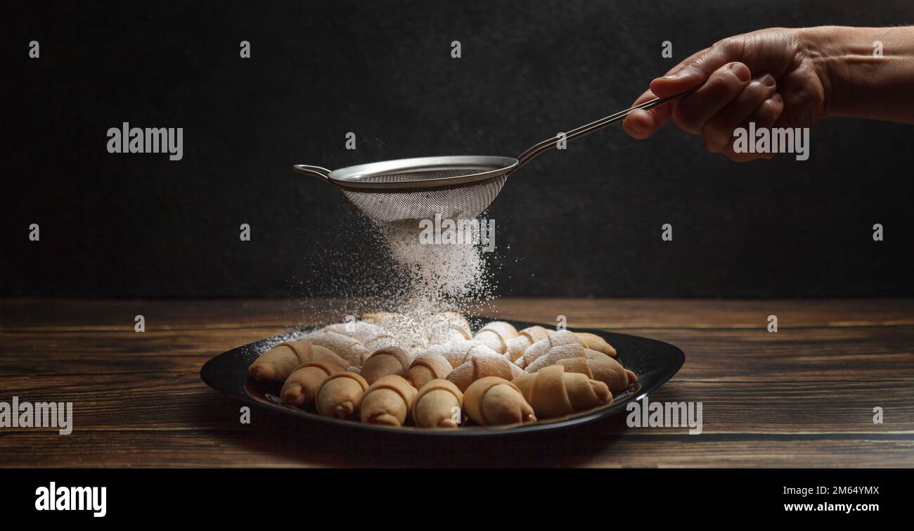 Womens hands sprinkle powdered sugar through a sieve on freshly baked ...
