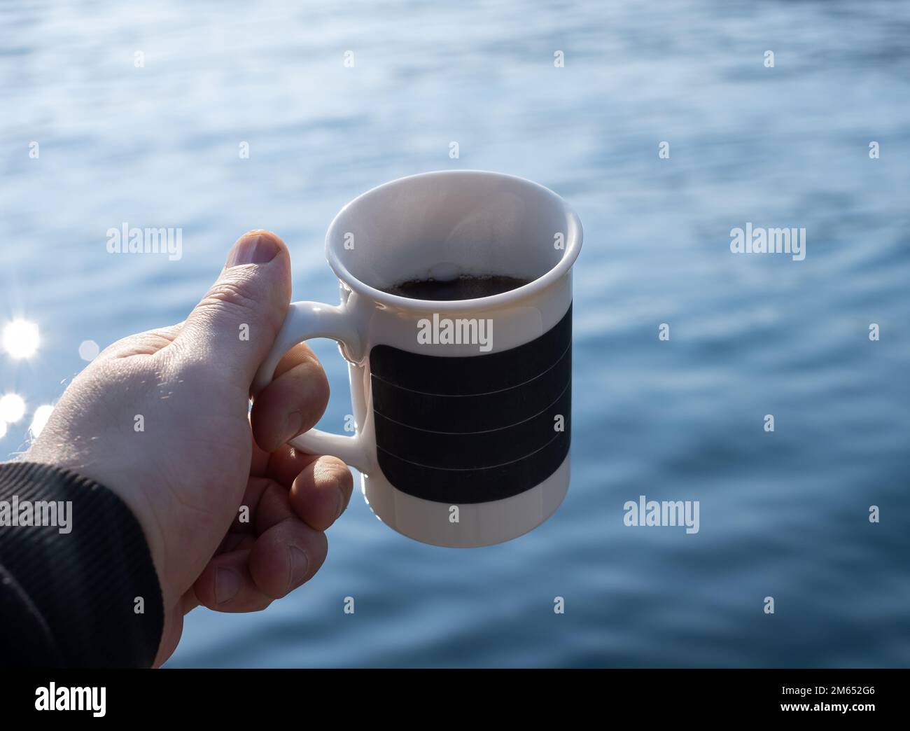 Cropped image of hand holding coffee cup against sea. Hand Holding ...