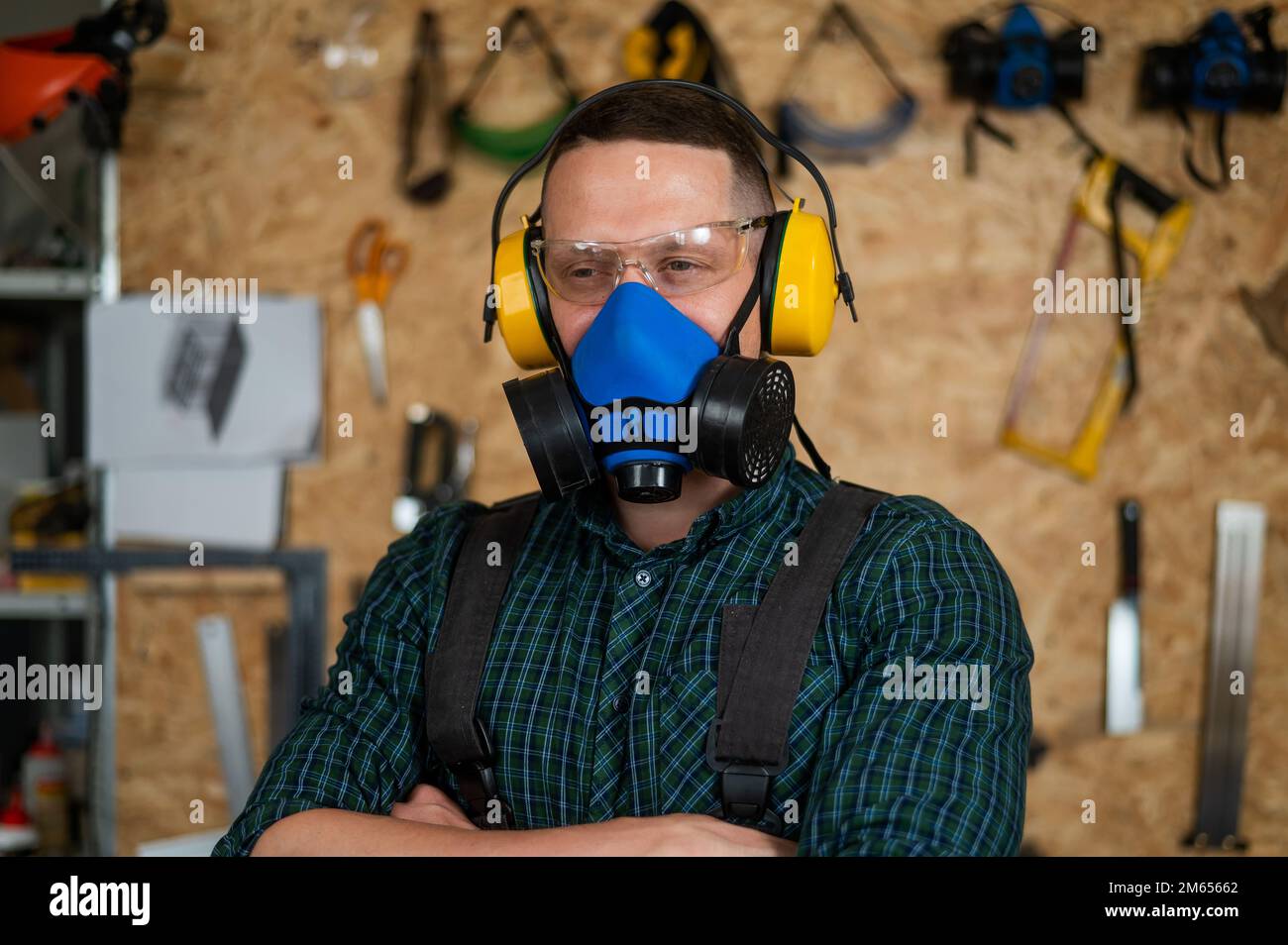 A carpenter in goggles, headphones and a respirator stands with his ...