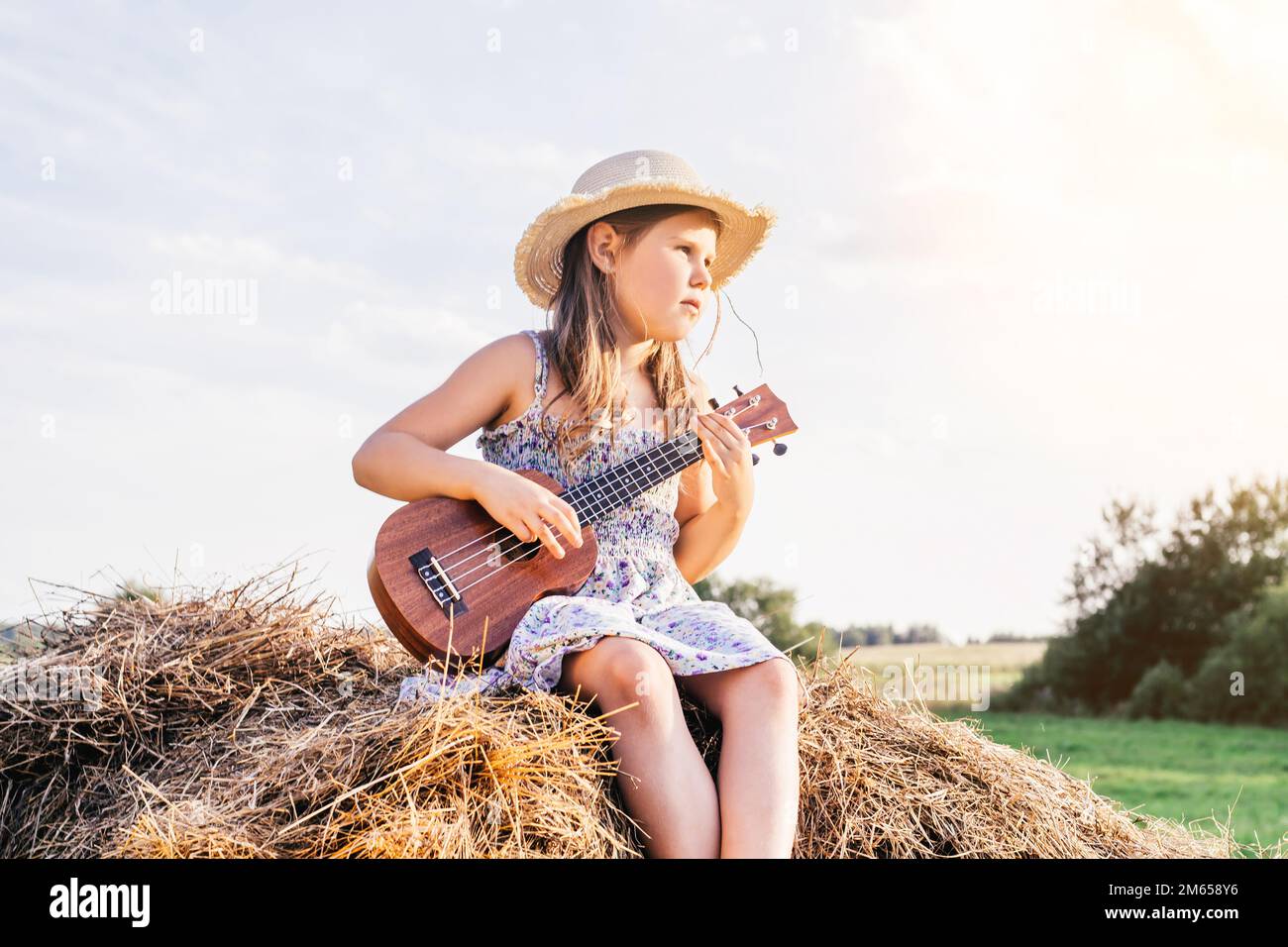 Pretty little girl in panama hat sit at top of haystack looking away ...