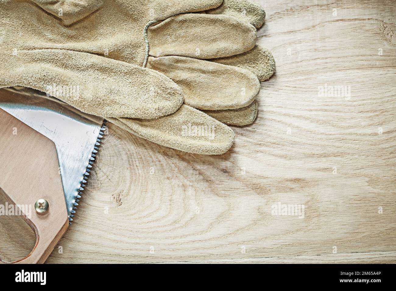 Pair of leather safety gloves sharp hacksaw on wooden board ...
