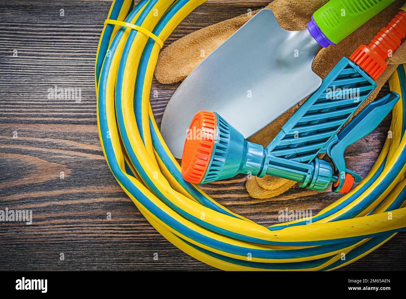 Twisted garden rubber hose safety gloves hand spade on wood board ...