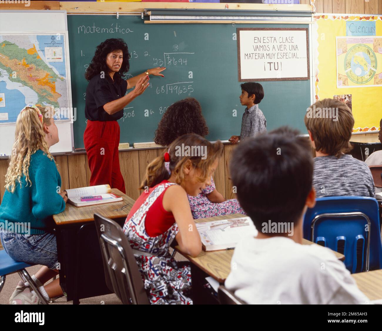 Hispanic woman teacher standing at the blackboard in a classroom full ... Hispanic woman teacher standing at the blackboard in a classroom full ...
