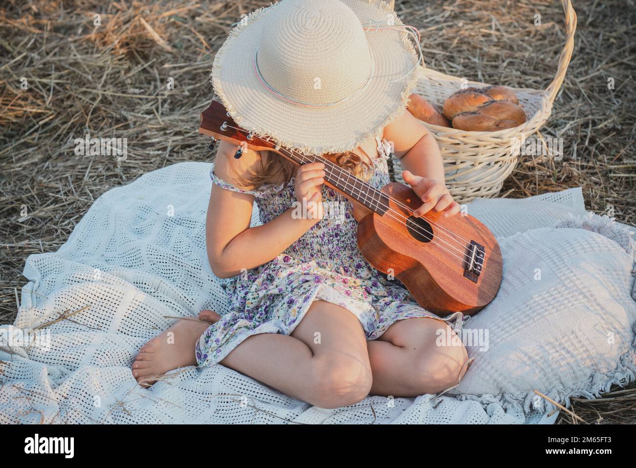 Little girl play ukulele sitting on blanket on field. Portrait of child ...