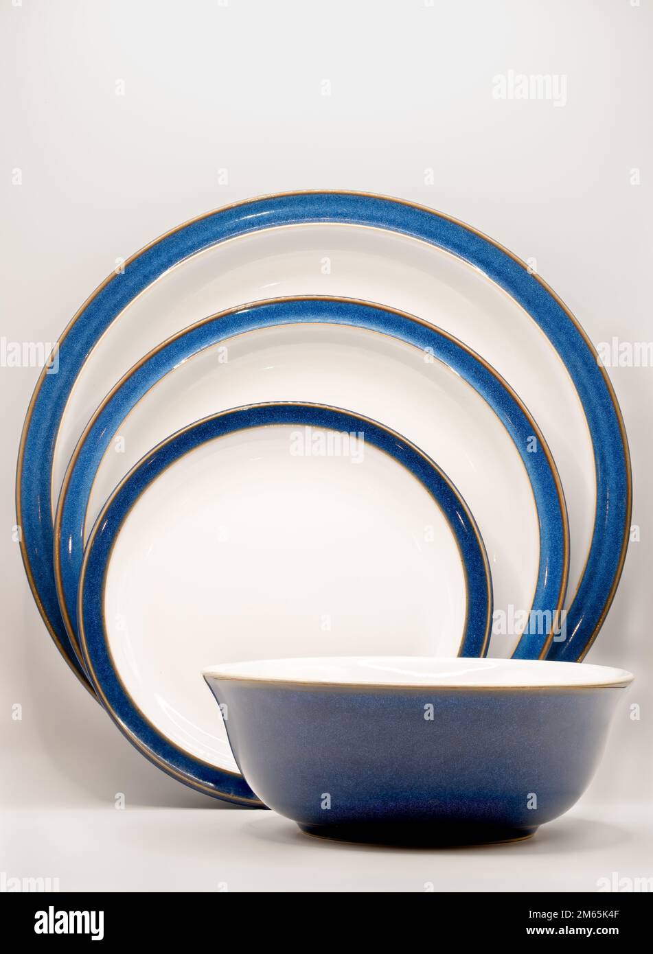 a bowl in front of three upright sizes of crockery plates in white with ...