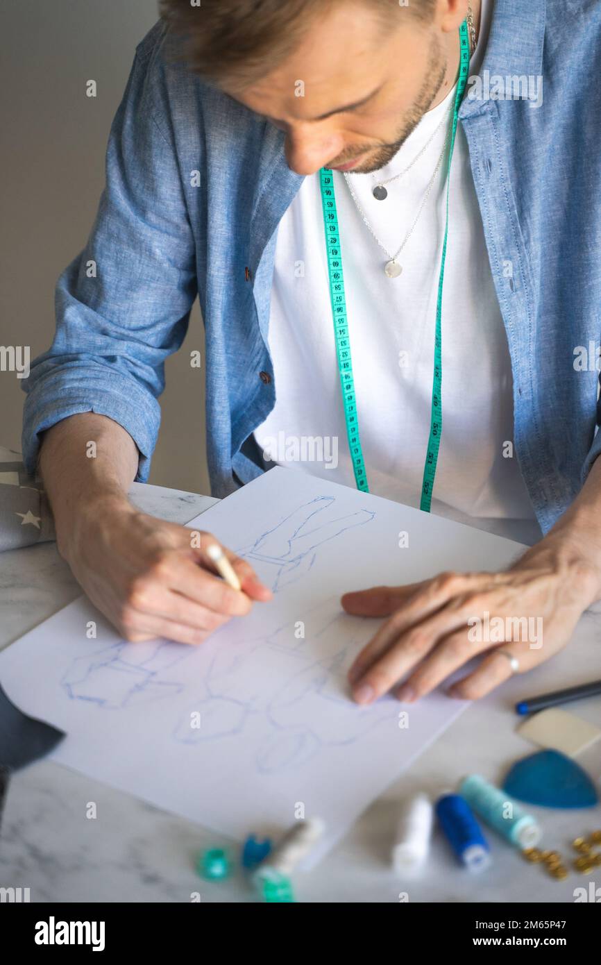 A man in a blue shirt makes a sketch for sewing clothes as a hobby. A ...