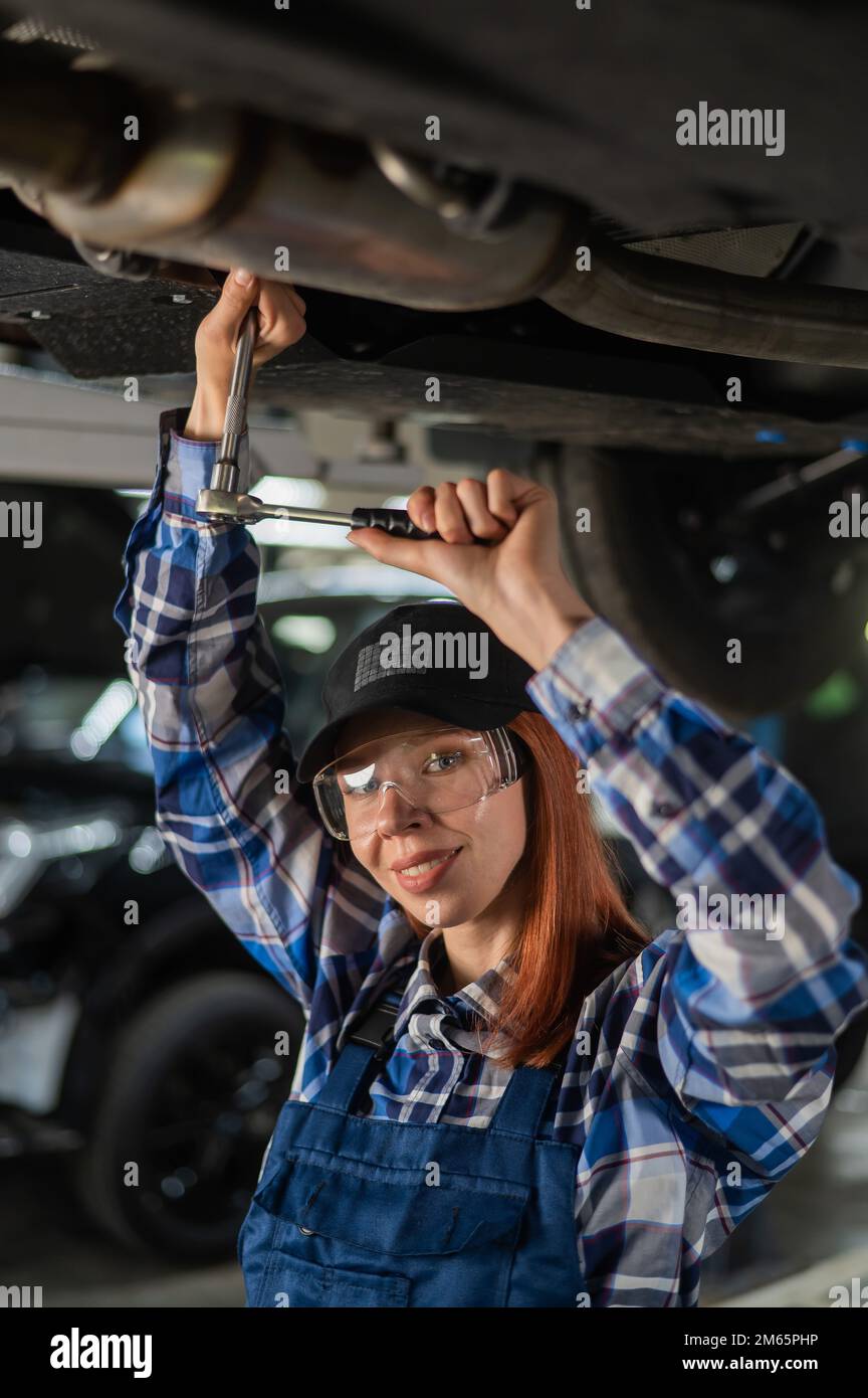 Female mechanic unscrew the nuts on the bottom of the car that is on ...