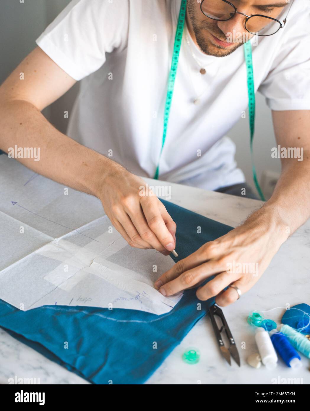 A self-taught tailor in white t-shirt and glasses works with fabric ...