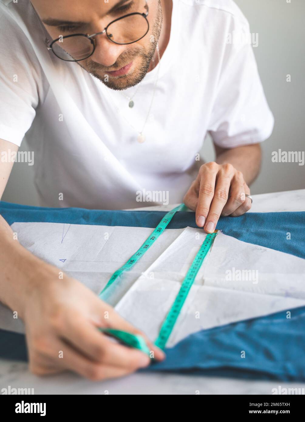 A tailor uses a measuring tape during his work in home workshop. A self ...