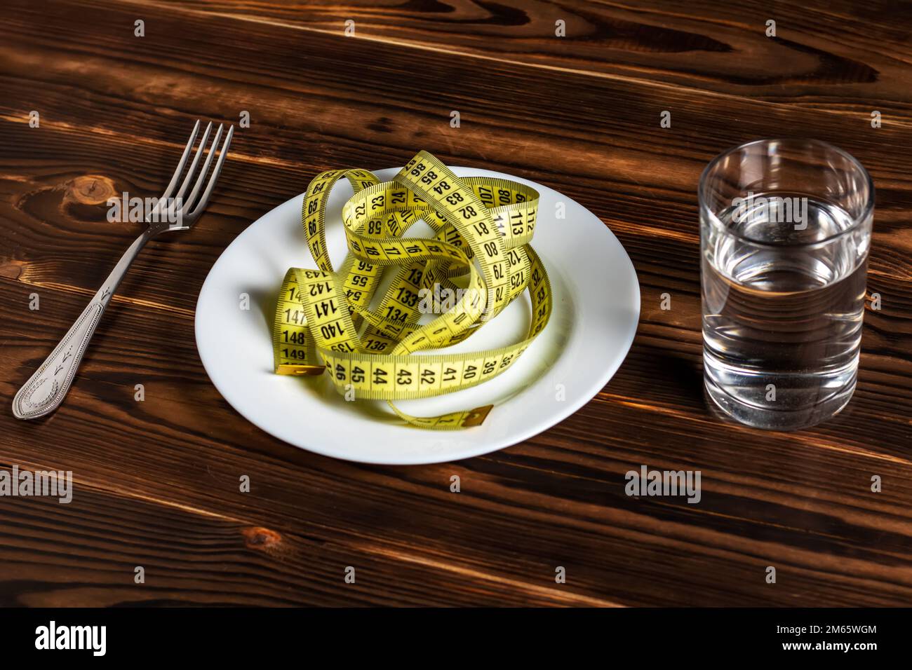 Diet concept. Empty plate with measuring tape, fork and glass with ...